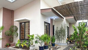 Pátio com plantas em vasos, um caminho de pedra e um edifício com janelas amplas e telhado inclinado.