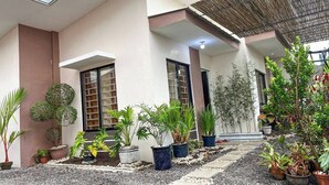 Um edifício moderno com área externa coberta, plantas em vasos e um caminho de cascalho.