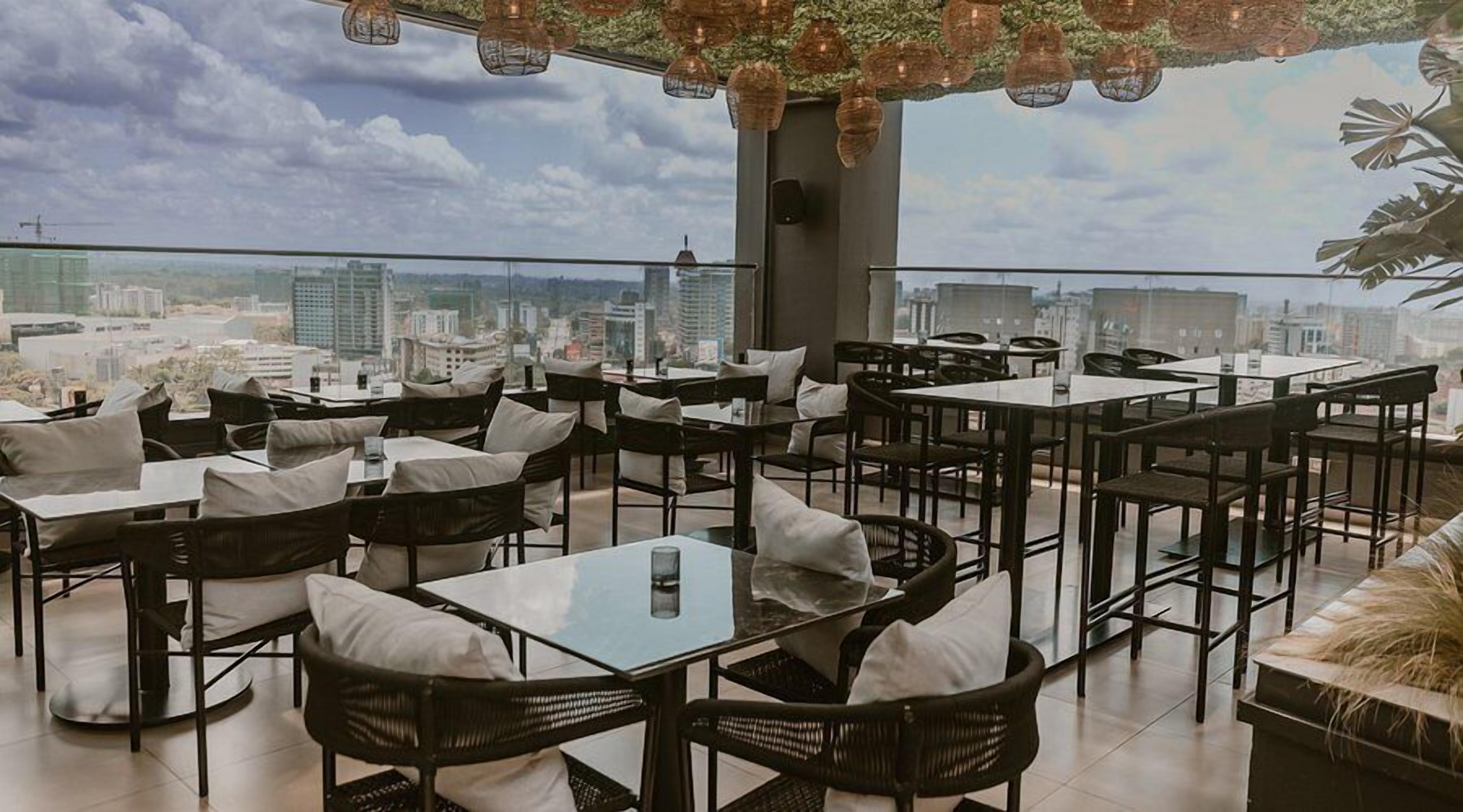 Um bar no terraço com mesas e cadeiras, com vista para a cidade.