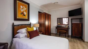 Quarto de hotel com uma cama, uma escrivaninha, um guarda-roupa, uma televisão e um quadro na parede.