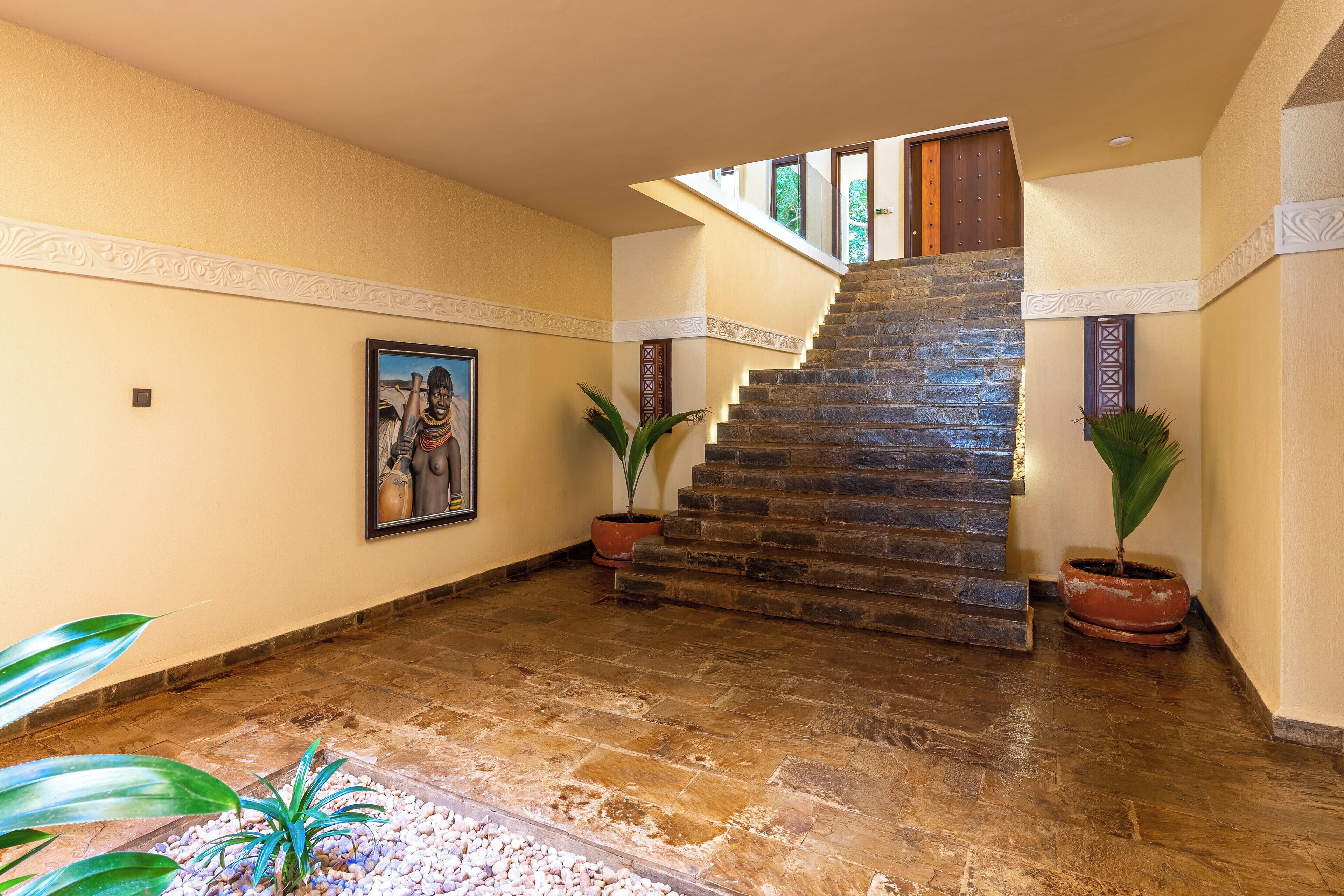 Um corredor com escadaria de pedra, plantas em vasos e um quadro na parede.