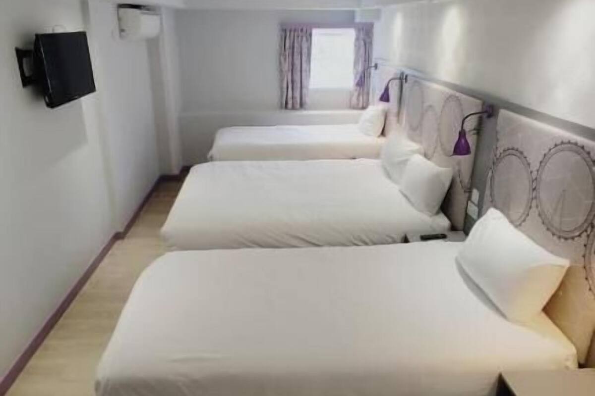 Quarto de hotel com três camas, televisão de tela plana e janela com cortinas.