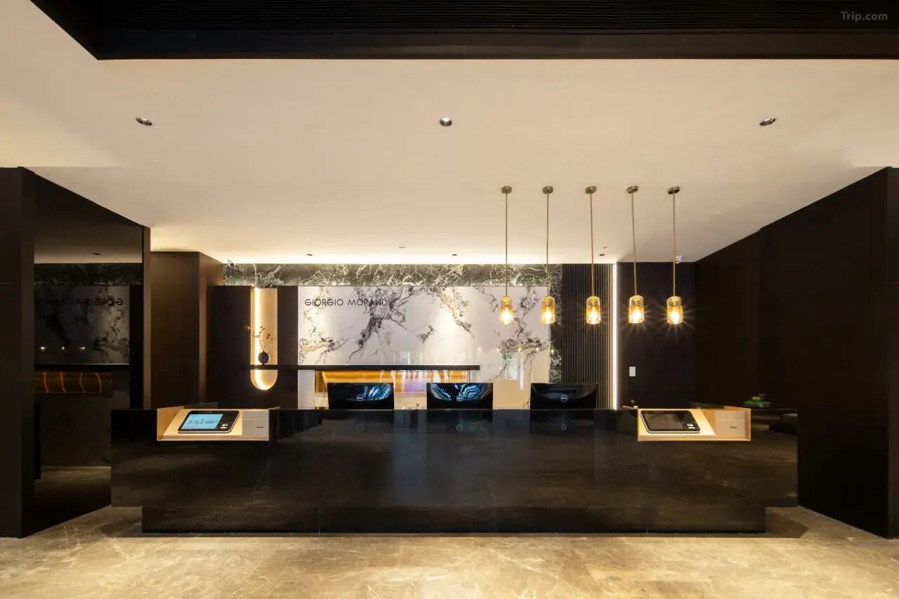 Uma área de recep ção moderna com parede de mármore, painel digital e luminárias pendentes.