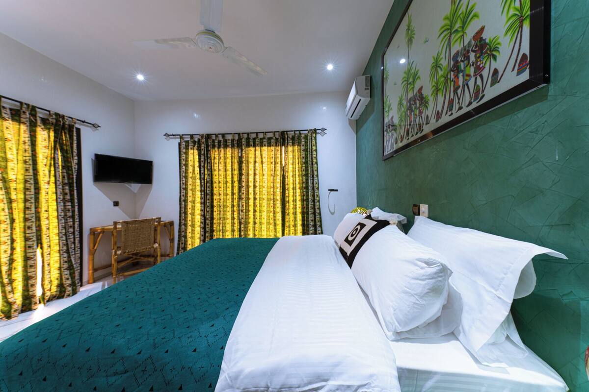 Quarto de hotel com uma cama, uma cadeira, uma televisão e um quadro na parede.