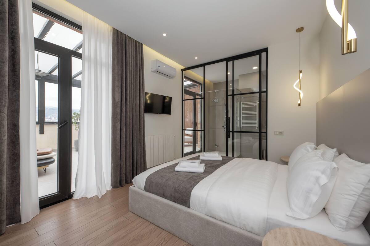 Quarto moderno com uma cama grande, uma televisão e uma porta de vidro deslizante que dá para uma varanda.