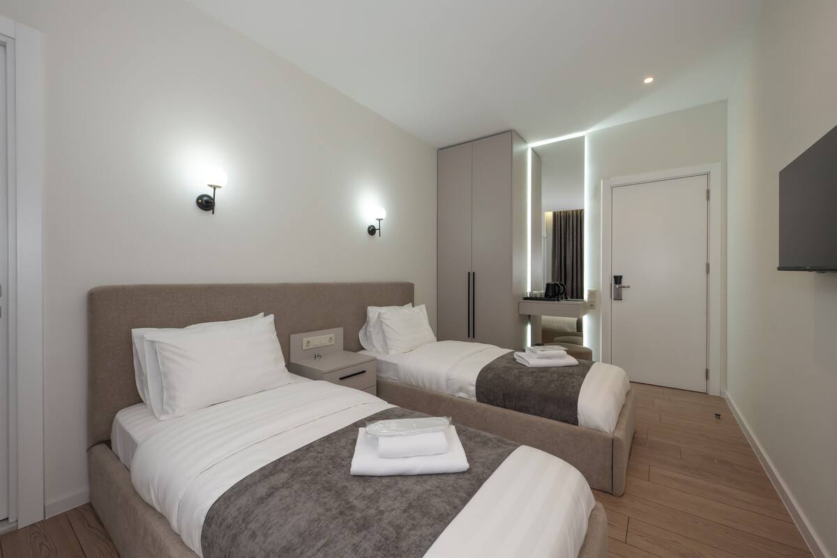 Quarto de hotel com duas camas, um guarda-roupa, um espelho e uma televisão.