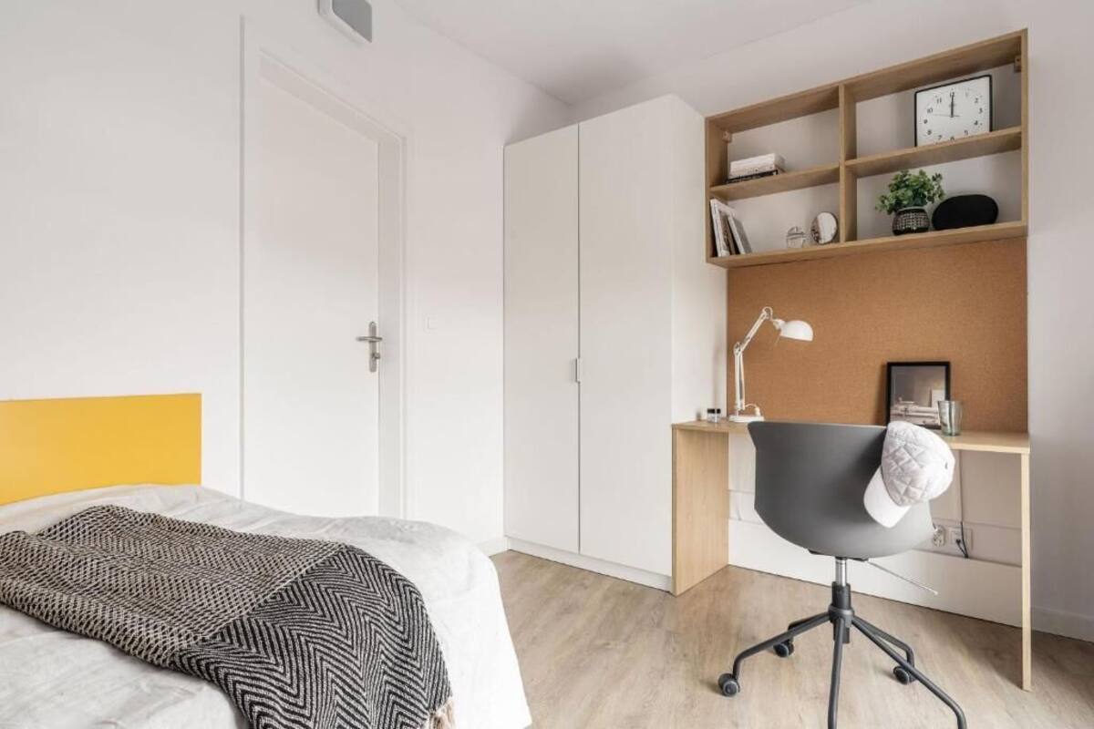 Um quarto com uma cama, escrivaninha, cadeira e guarda-roupa.