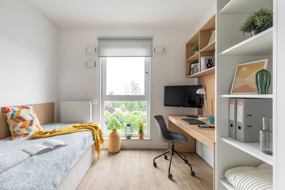 Quarto moderno com cama, escrivaninha, cadeira e janela com vista.