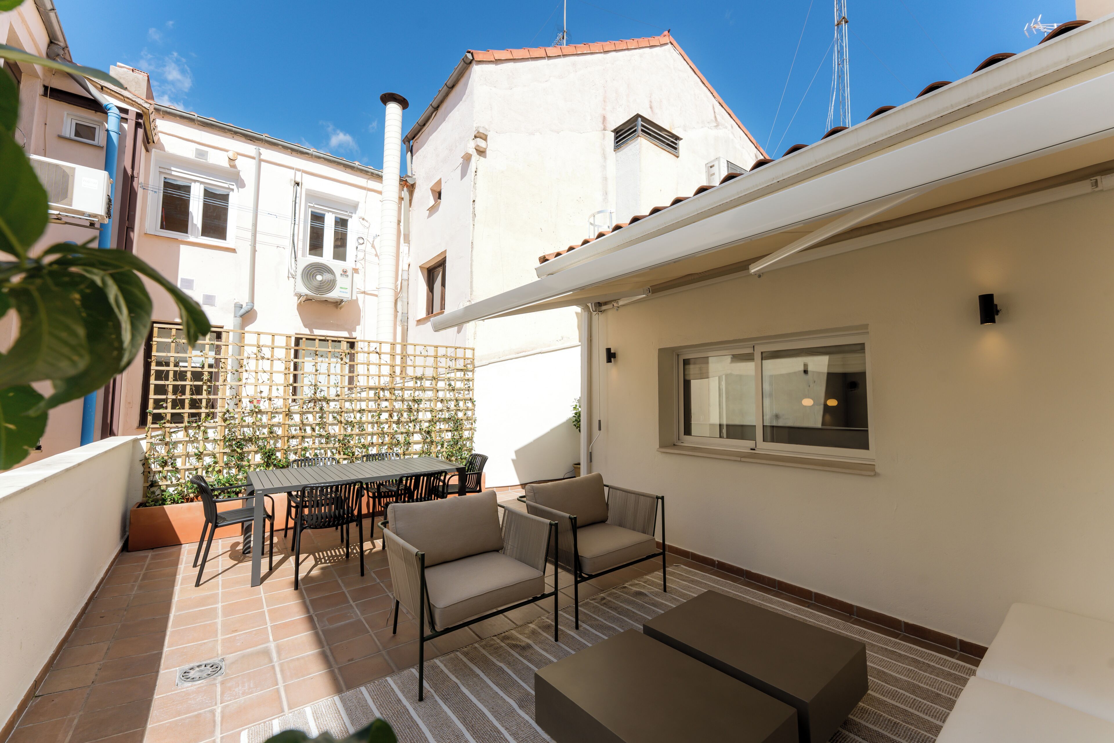 Um pátio com mesa e cadeiras, um pequeno jardim e um edifício com telhado de azulejos.
