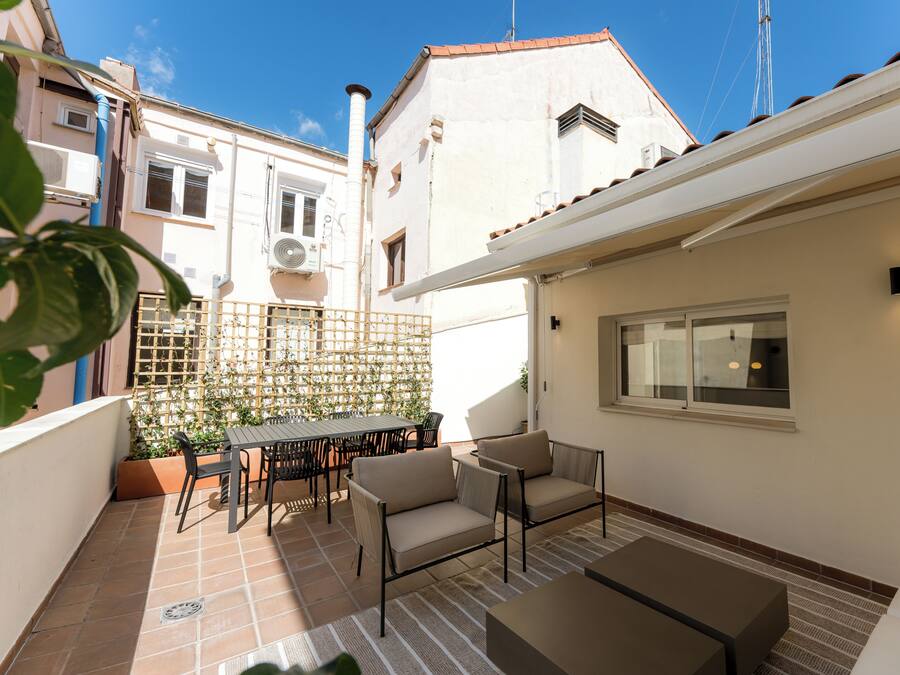 Um pátio com mesa e cadeiras, um pequeno jardim e um edifício com telhado de azulejos.