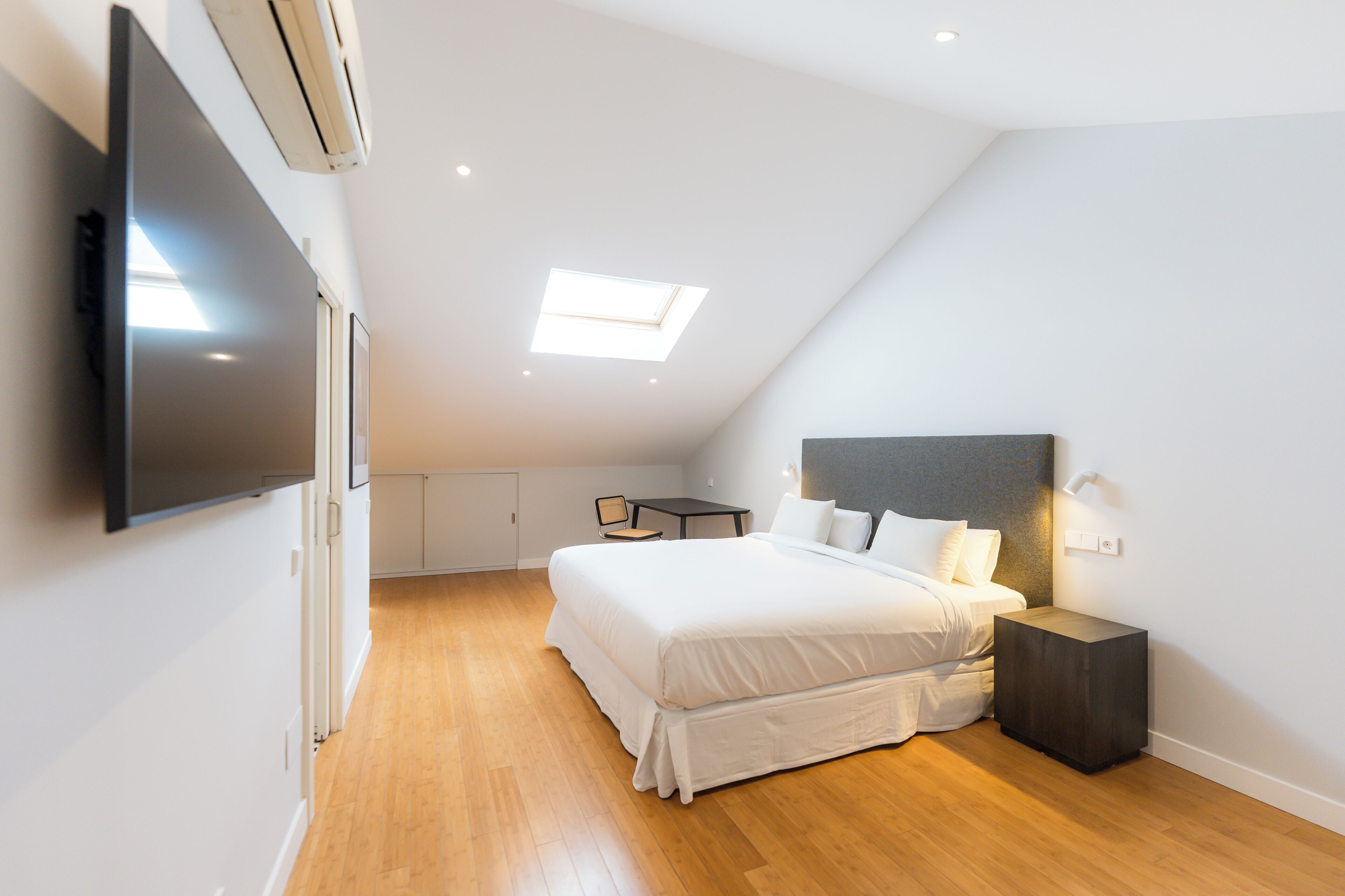 Quarto moderno com cama, mesa de cabeceira e televisão na parede.