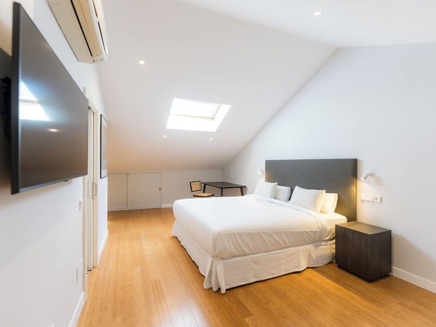 Quarto moderno com cama, mesa de cabeceira e televisão na parede.