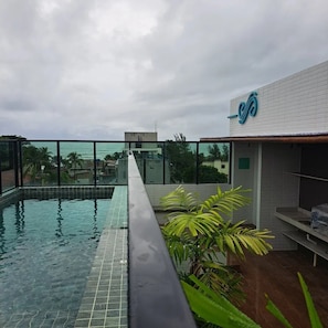 Piscina no terraço com vista para o oceano e palmeiras.