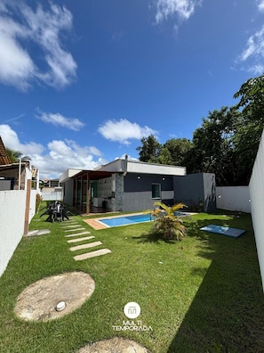 Uma casa moderna com piscina, gramado bem cuidado e área de varanda.