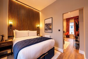 Quarto moderno com uma cama grande, parede de painéis de madeira, um quadro emoldurado e vista para uma sala de jantar.