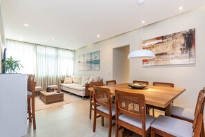 Uma sala de estar moderna com área de jantar, apresentando uma mesa de jantar de madeira, cadeiras, um sofá e uma mesa de centro.