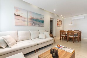 Uma sala de estar moderna com um sofá bege, uma mesa de centro de madeira e uma área de jantar com cadeiras de madeira.