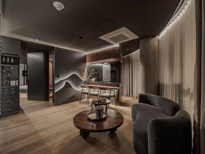 Uma sala de estar moderna com uma mesa de centro de madeira, um sofá, uma área de refeições com mesa e cadeiras, e uma cozinha com frigorífico e armários.