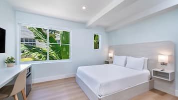 Quarto moderno com cama, mesas de cabeceira, escrivaninha e uma janela grande com vista para o verde.