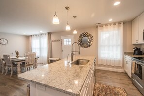Uma cozinha moderna com bancada de granito, eletrodomésticos de aço inoxidável, iluminação pendente e uma área de jantar com mesa e cadeiras.