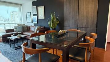 Uma área de refeições moderna com uma mesa de vidro, cadeiras de madeira e um lustre singular.