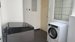 Uma lavanderia com máquina de lavar e secadora, uma porta com uma pequena janela e um teto com sistema de ventilação.