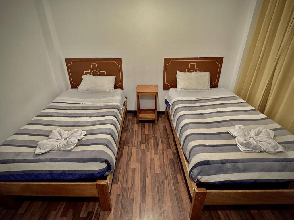 Quarto de hotel com duas camas de solteiro, cabeceiras de madeira, uma pequena mesa de cabeceira de madeira e piso de madeira.