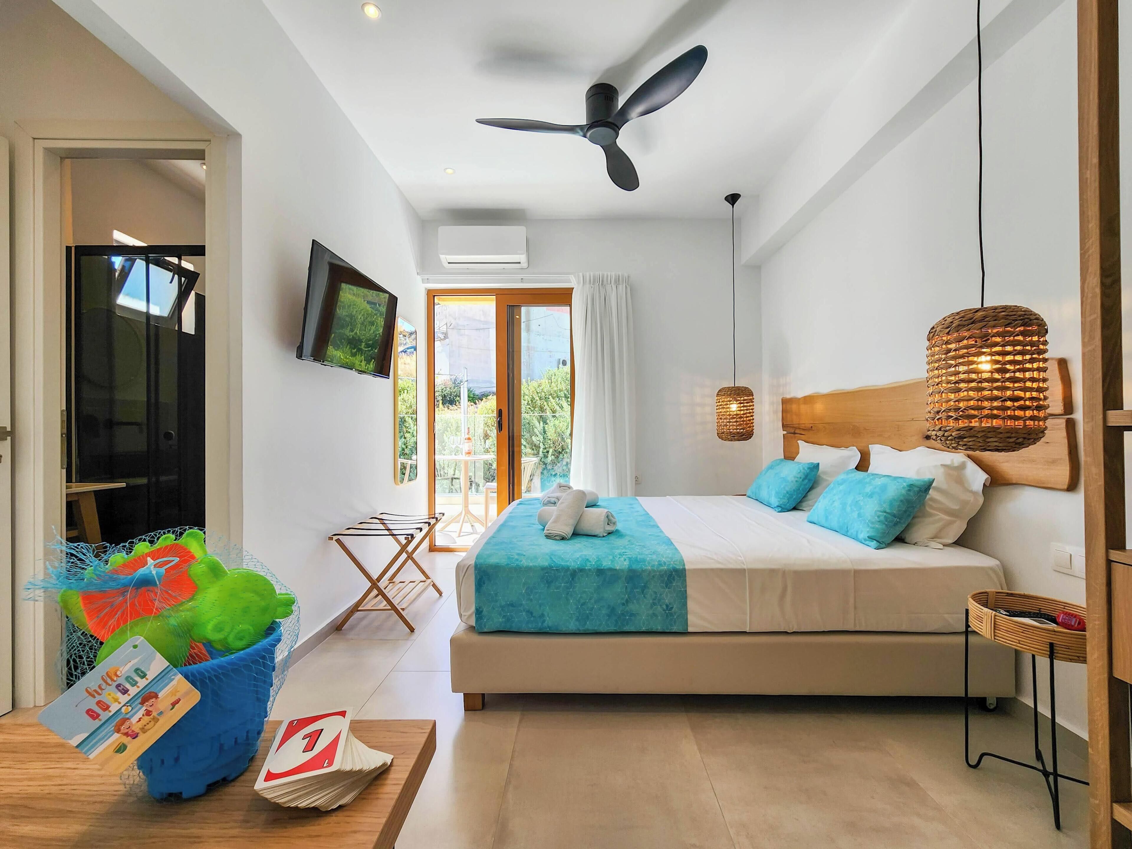 Quarto moderno com cama, ventoinha no teto, TV e vista para o exterior.