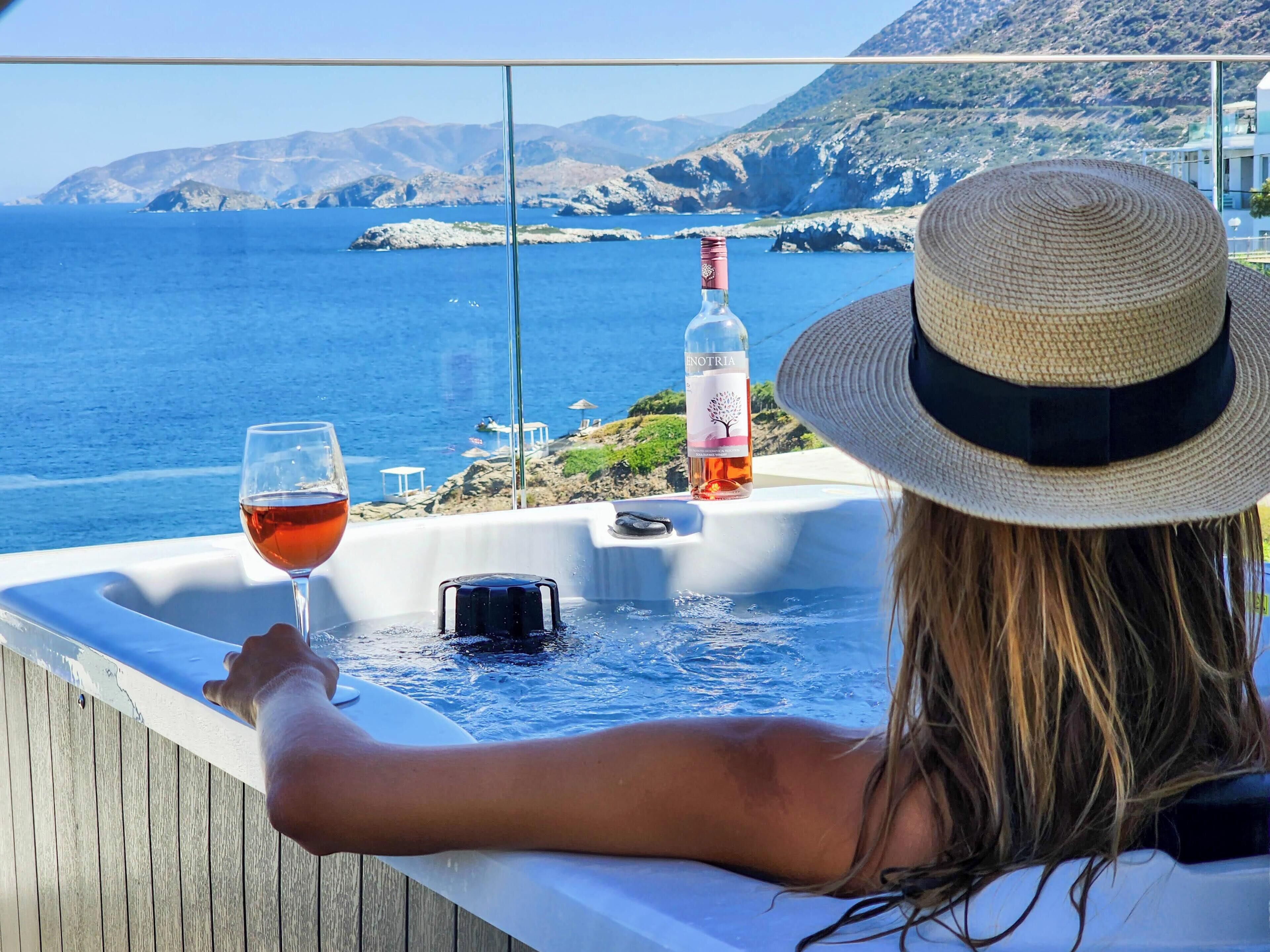Alguém relaxa perto de uma janela com vista para o mar, uma garrafa de vinho e um copo de vinho sobre uma mesa.