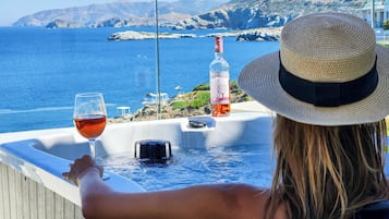 Alguém relaxa perto de uma janela com vista para o mar, uma garrafa de vinho e um copo de vinho sobre uma mesa.