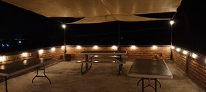 Uma área de pátio ao ar livre com mesas e bancos, iluminada por luzes de Natal.