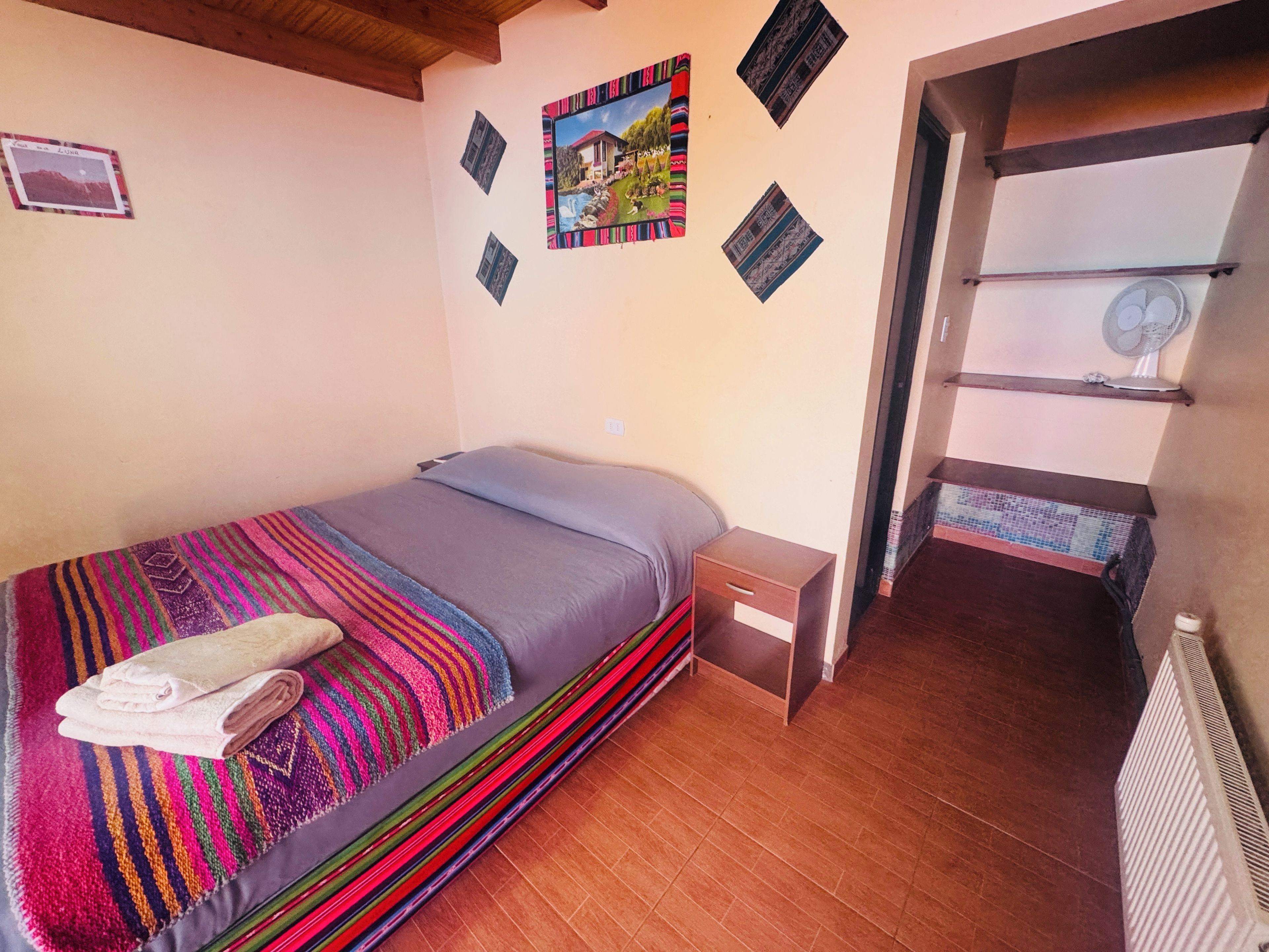Quarto com uma cama, mesa de cabeceira, prateleira na parede e radiador.