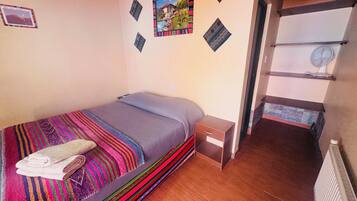 Quarto com uma cama, mesa de cabeceira, prateleira na parede e radiador.