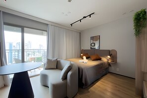 Um quarto moderno com cama, sofá, uma mesinha e vista para a cidade.