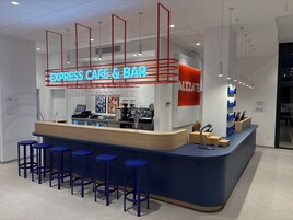 Café e bar modernos com letreiro de neon, banquetas, máquina de café e balcão com um computador.