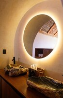 Casa de banho com espelho redondo, bancada de madeira e porta-toalhas.
