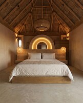 Quarto com cama grande, cabeceira de madeira e teto de palha.