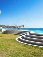 Uma área ajardinada com piscina, gramado e vista para o oceano.