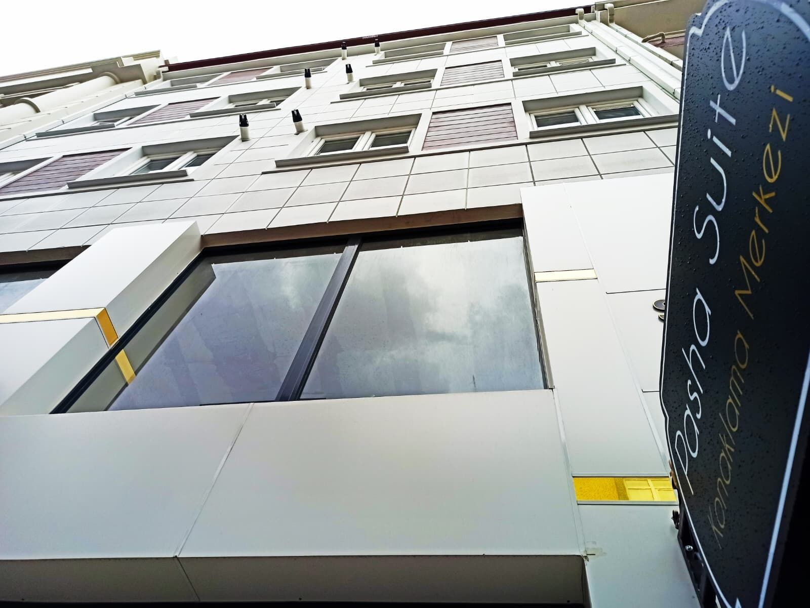 Um edifício com design arquitetônico moderno, destacando uma entrada imponente com fachada de vidro e uma placa indicando "Pensione Merkez".