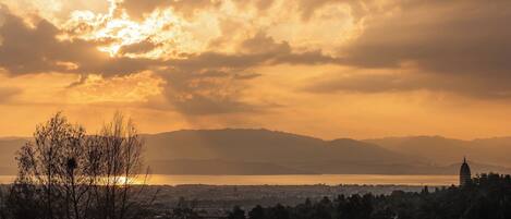 Vista panorâmica de uma paisagem urbana com uma pagoda imponente, um corpo d'água e montanhas ao longe sob um céu ao pôr do sol.