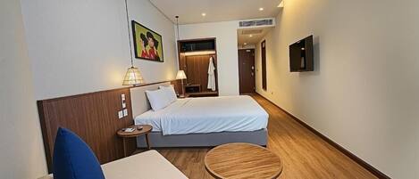 Quarto de hotel moderno com cama, mesa de cabeceira, abajur e uma mesa redonda de madeira.