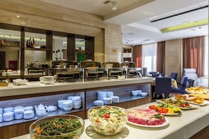Buffet variado com diversos pratos, incluindo saladas e um prato com carne, em um hotel moderno.
