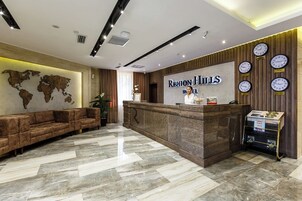Uma área de recepção de hotel com piso de mármore, balcão de atendimento, um mapa-múndi na parede e vários relógios.