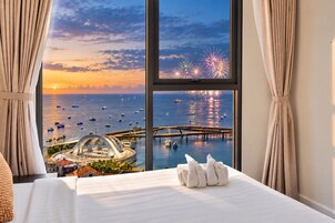 Quarto de hotel com uma grande janela com vista para um areal, uma ponte e fogos de artifício.