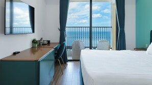 Quarto de hotel com cama, escrivaninha, cadeira e varanda com vista para o mar.