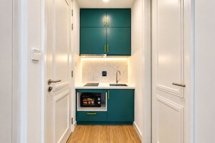 Corredor estreito que dá para uma cozinha com armários azul-turquesa, forno embutido e painel de fundo de mármore.