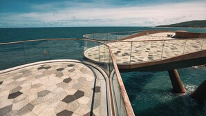 Um terraço com piso estampado, guarda-corpo de vidro e vista para o mar.