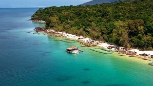 Vista aérea de uma área costeira com águas azul-turquesa cristalinas, um pequeno barco e uma praia com vegetação densa.