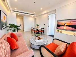 Uma sala de estar moderna com sofá, cadeiras, mesa de centro redonda e TV na parede.