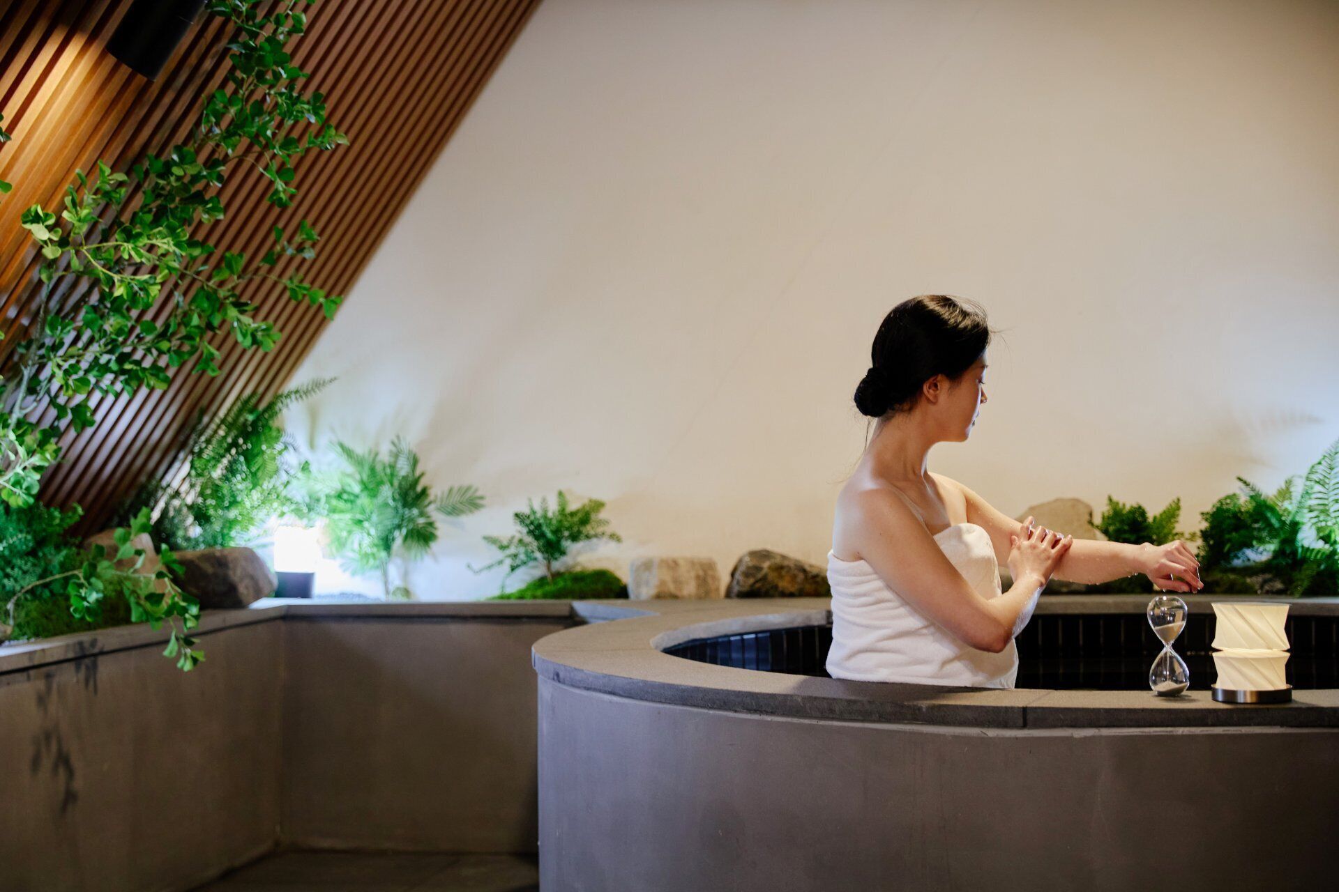 Uma área de spa com banheira de pedra quente, ripas de madeira e vegetação.
